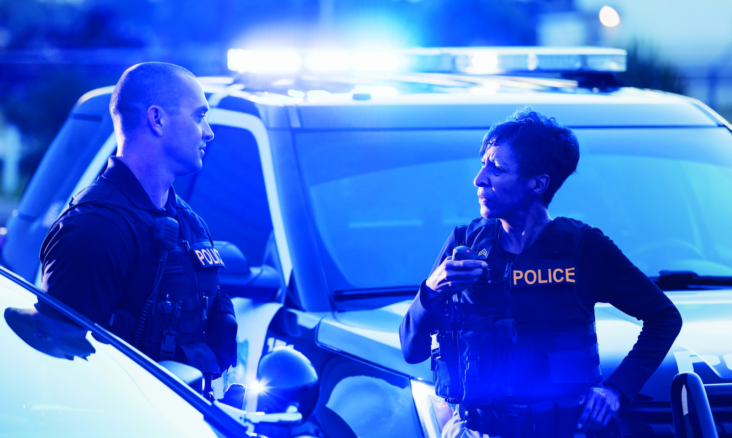 Two police officers by their patrol cars, on radio - Police Chief Magazine