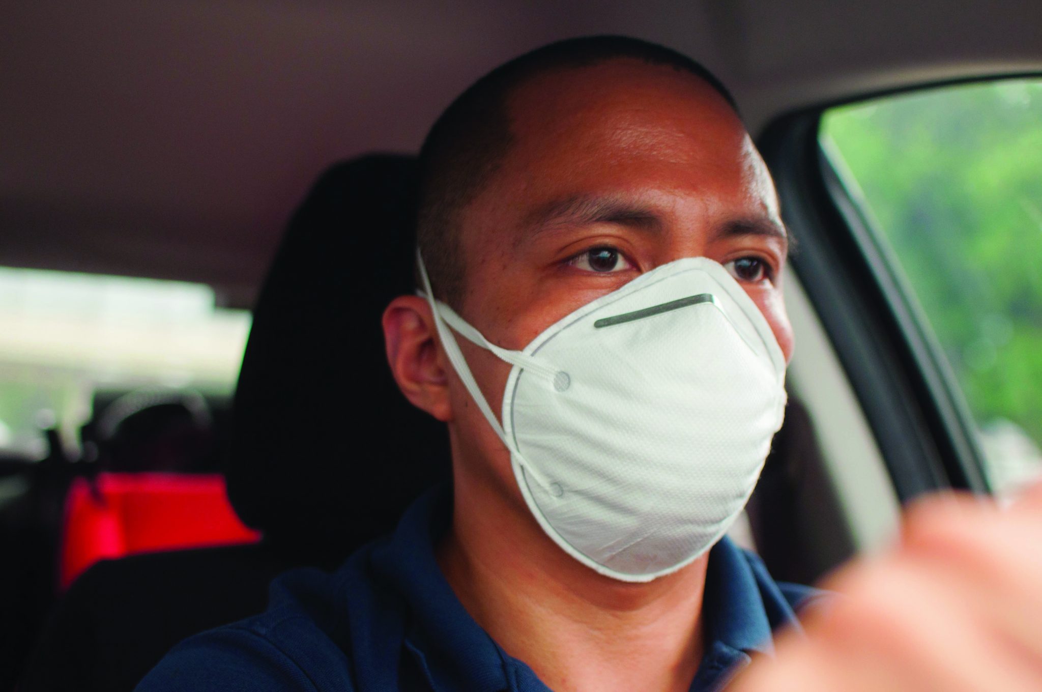 A young Southeast Asian man with a protective mask is driving a car ...