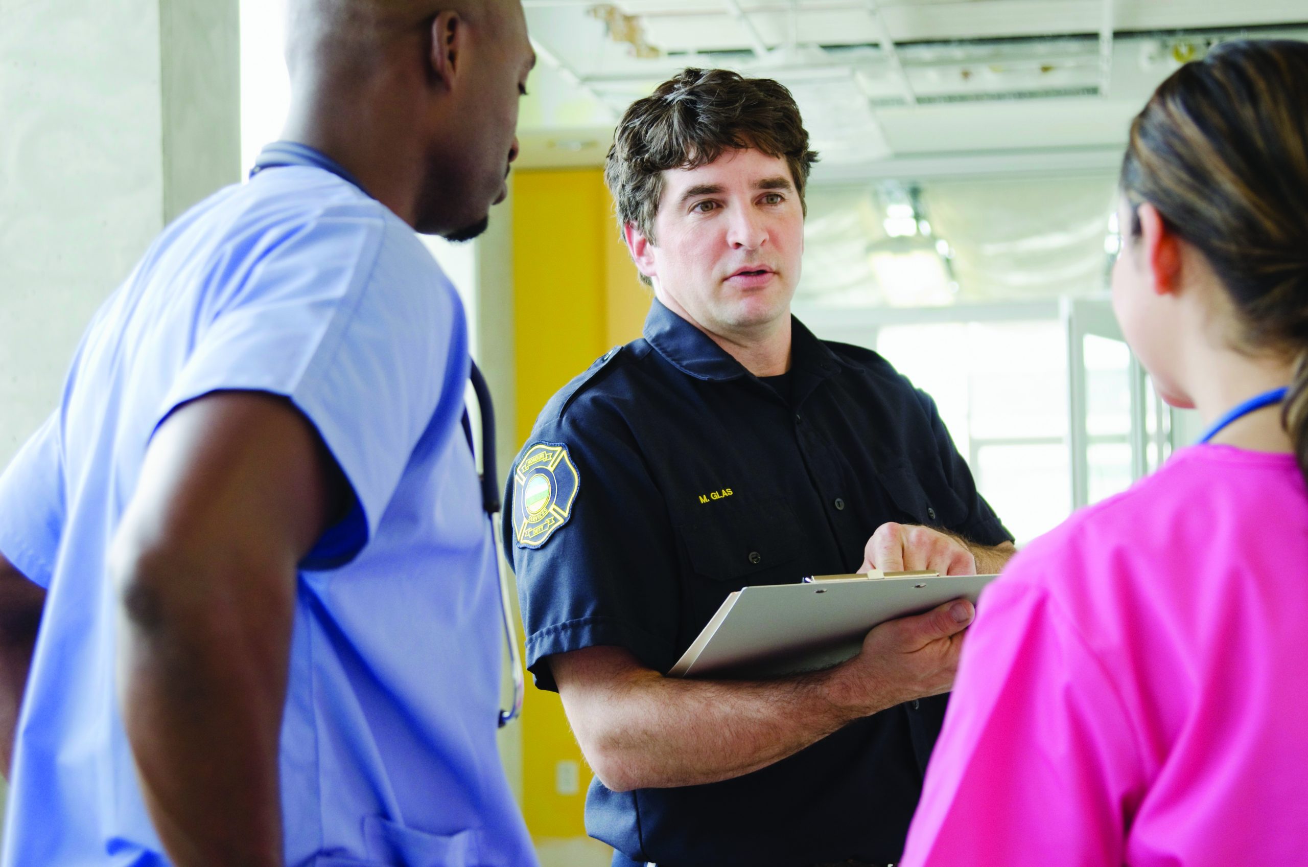 Man in uniform talking to female and male nurses in hospital corridor ...